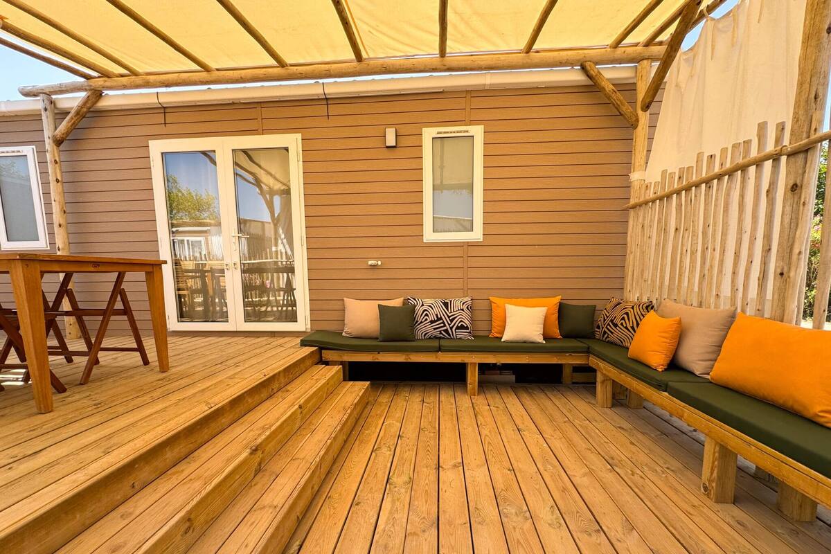 Um deck de madeira com um banco e uma mesa, uma porta de correr com vidro e um cercado de madeira.