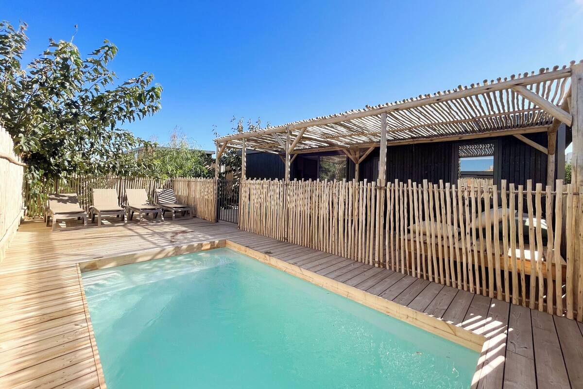 Um deck de madeira com piscina, área de estar coberta e cerca de madeira.