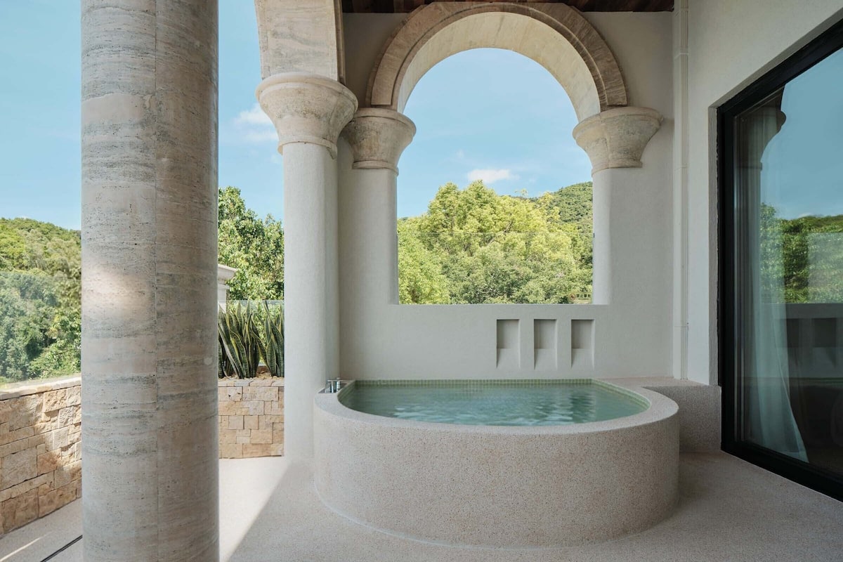 Uma área de spa com hidromassagem, colunas de pedra e vista para uma encosta arborizada.
