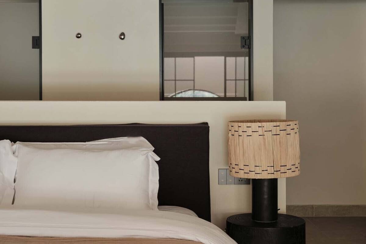 Quarto de hotel com cama, cabeceira, aquecedor fixado na parede e luminária.