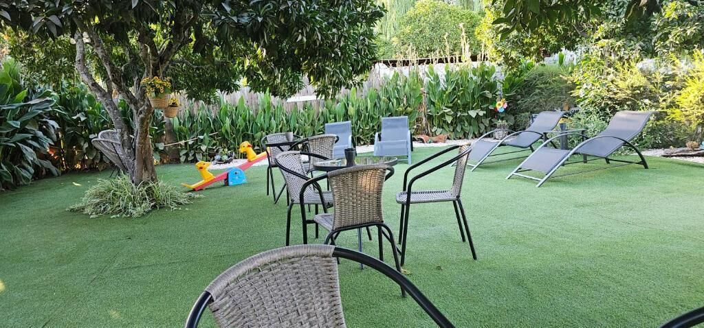 Uma área de pátio com mobiliário externo, uma pequena estrutura de recreação e vegetação exuberante.