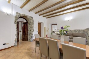 Uma área de refeições com arco de pedra, vigas de madeira, piso ladrilhado e uma mesa com cadeiras.