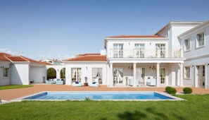 Um grande edifício branco com piscina, área de estar externa e um gramado bem cuidado.