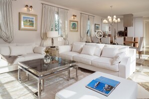 Uma sala de estar moderna com um sofá branco, uma mesa de centro de vidro e uma área de jantar com um candelabro.