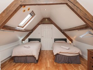 Quarto com duas camas, vigas de madeira, claraboia e porta branca.