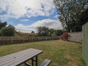 Uma mesa de piquenique em um quintal gramado com um muro de pedra e uma cerca de madeira.