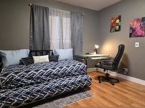 Quarto com cama, escrivaninha, cadeira e duas pinturas na parede.