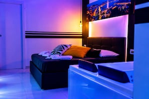 Quarto moderno com cama, almofadas, mesa de cabeceira e criado-mudo.