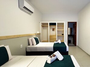 Quarto de hotel com duas camas, um guarda-roupa e um banheiro visível através de uma porta aberta.