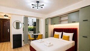 Quarto de hotel com cama, escrivaninha, cadeiras, espelho e guarda-roupa.