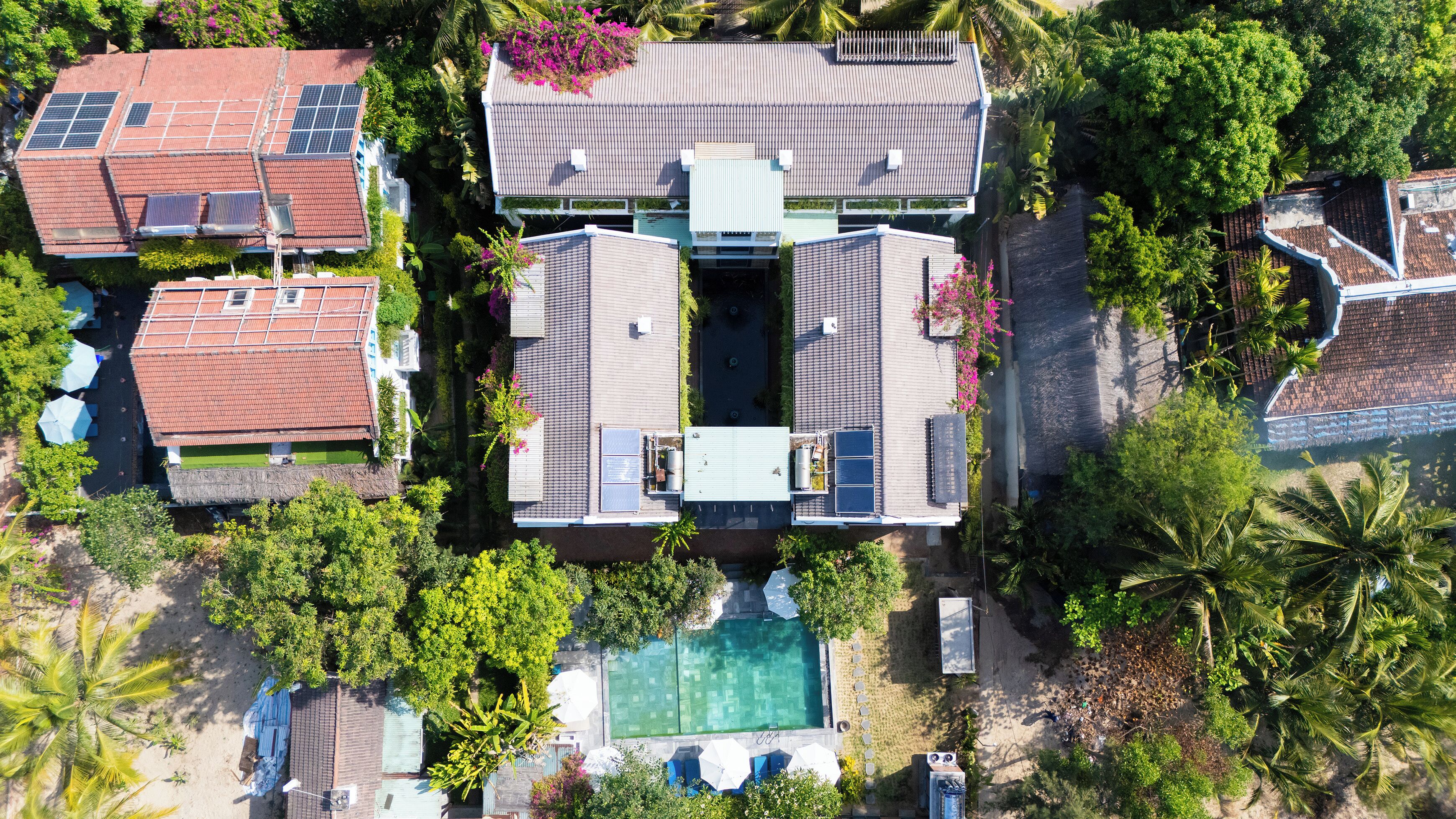 Vista aérea de um bairro residencial com várias casas, uma piscina e vegetação exuberante.