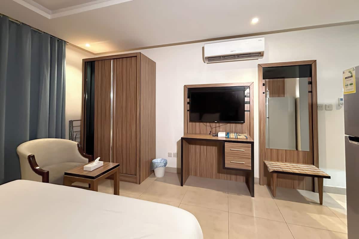 Quarto de hotel com cama, escrivaninha com computador, televisão, espelho e ar condicionado.