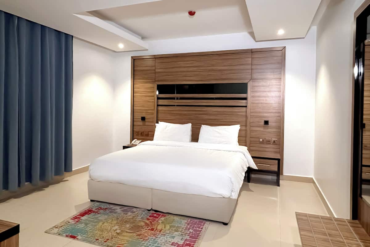 Quarto de hotel moderno com uma cama grande, cabeceira de madeira e um tapete estampado.