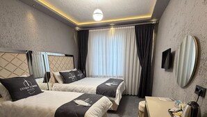 Quarto de hotel com duas camas, uma escrivaninha, um espelho e uma janela com cortinas.