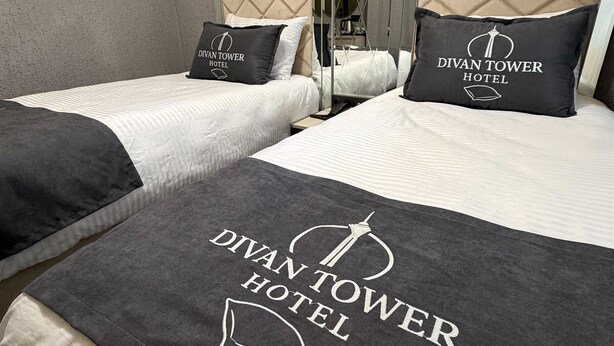 Quarto de hotel com duas camas, cada uma com travesseiro exibindo o logotipo do hotel. O quarto possui uma parede texturizada e uma cabeceira moderna.