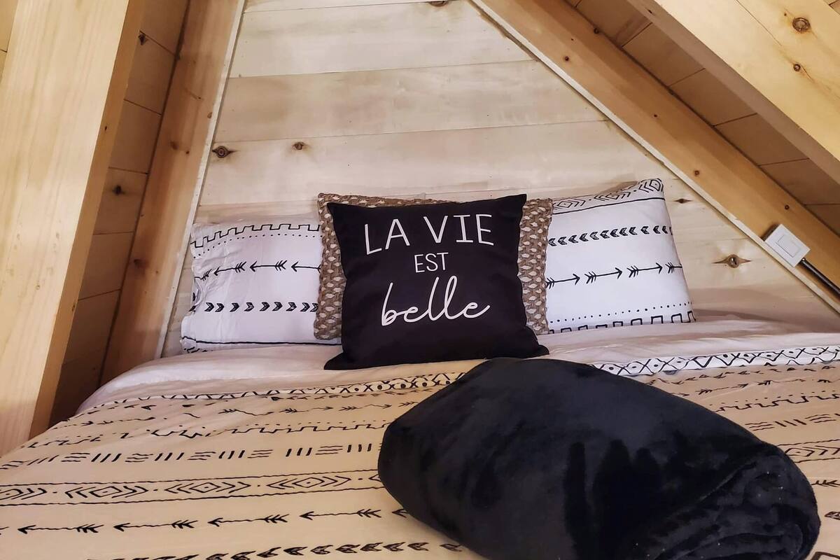 Quarto com teto inclinado, cama com roupa de cama estampada e almofadas decorativas.