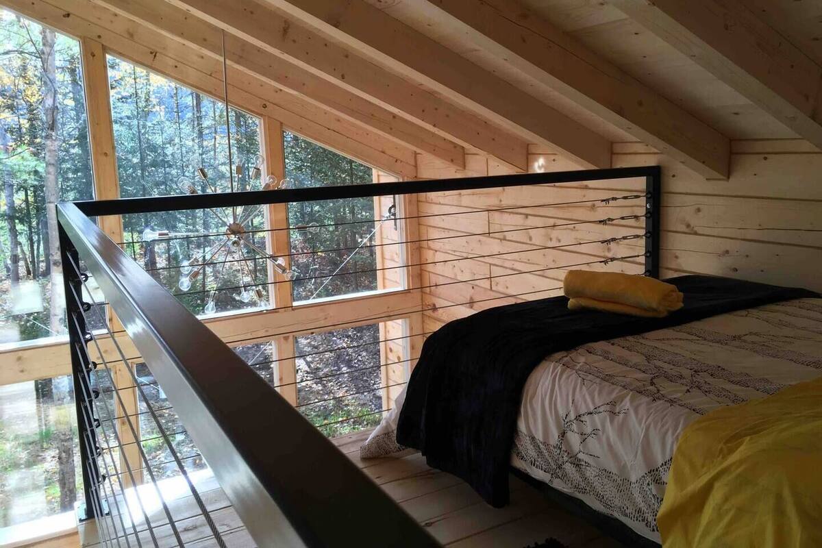 Quarto de cabana de madeira com cama, janela e grade de varanda.