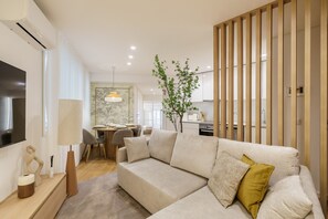 Uma sala de estar moderna com sofá, televisão, abajur e um espaço de jantar ao fundo.