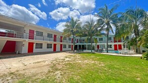 Um edifício de dois andares com portas e janelas vermelhas, área de estar coberta ao ar livre e piscina.