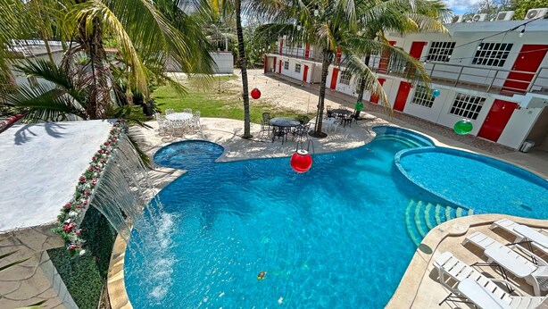 Piscina com duas áreas distintas, rodeada por palmeiras e mobiliário de exterior.