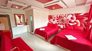 Quarto de hotel com duas camas, um grande mural floral na parede, banheiro com chuveiro e uma mesa com cadeira.