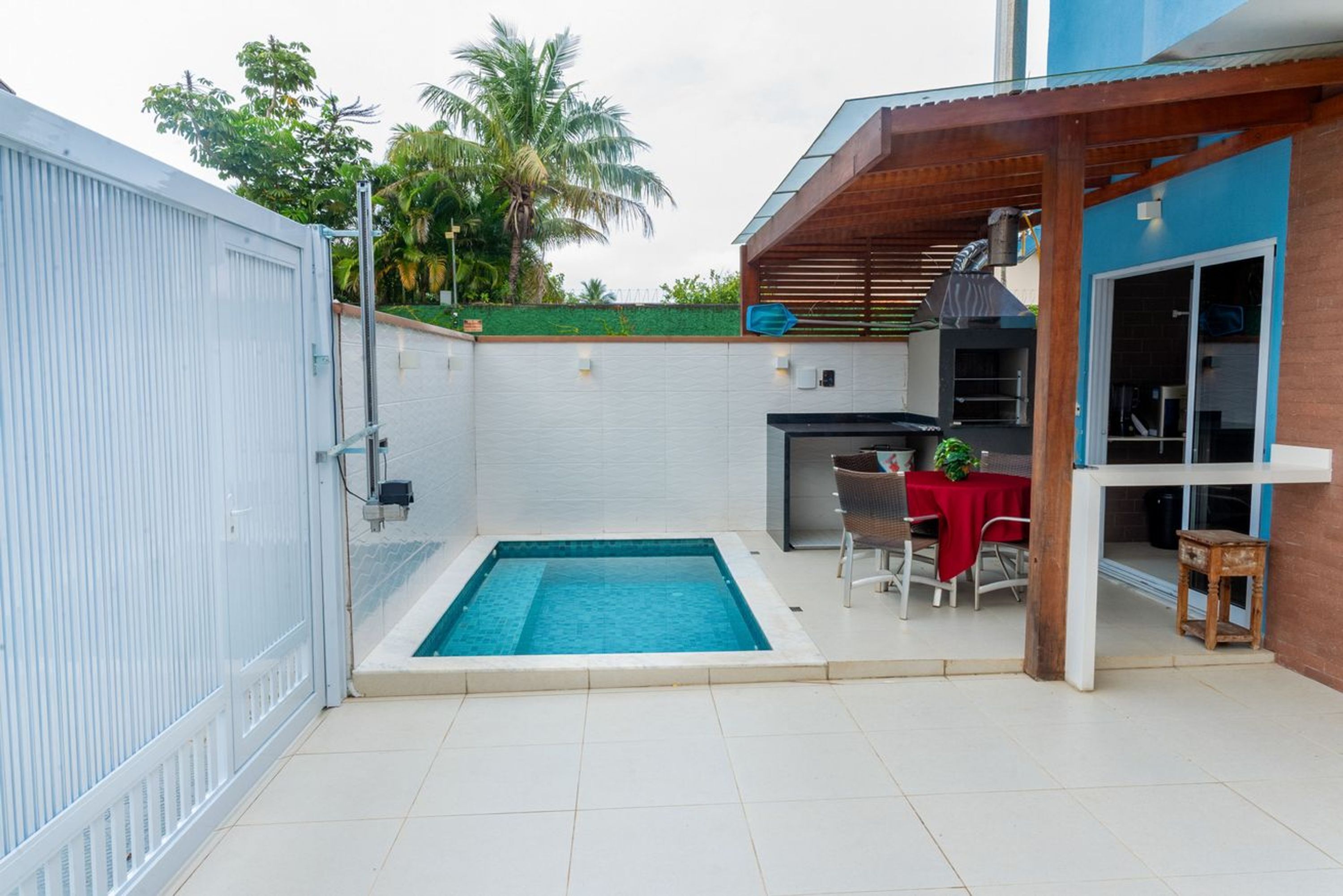 Uma piscina, um terraço coberto e uma mesa de jantar com cadeiras.