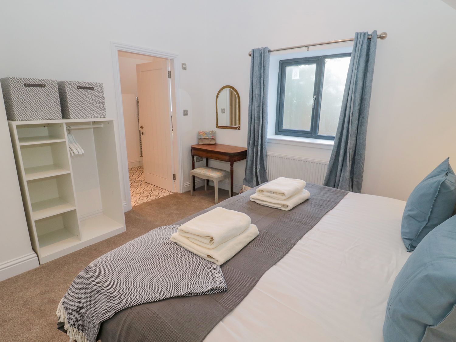 Quarto com cama, escrivaninha, guarda-roupa e janela com cortinas.