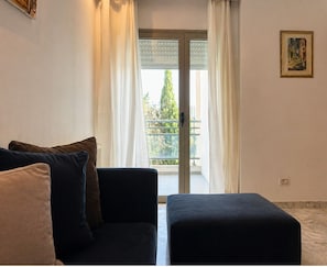 Uma sala de estar com sofá, banquinho e varanda com vista.