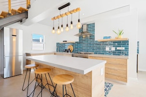 Uma cozinha moderna com uma ilha central, banquetas, geladeira de aço inoxidável e painel de azulejos azuis.