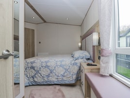 Quarto com cama, mesa de cabeceira, abajur, janela e vista para o exterior.