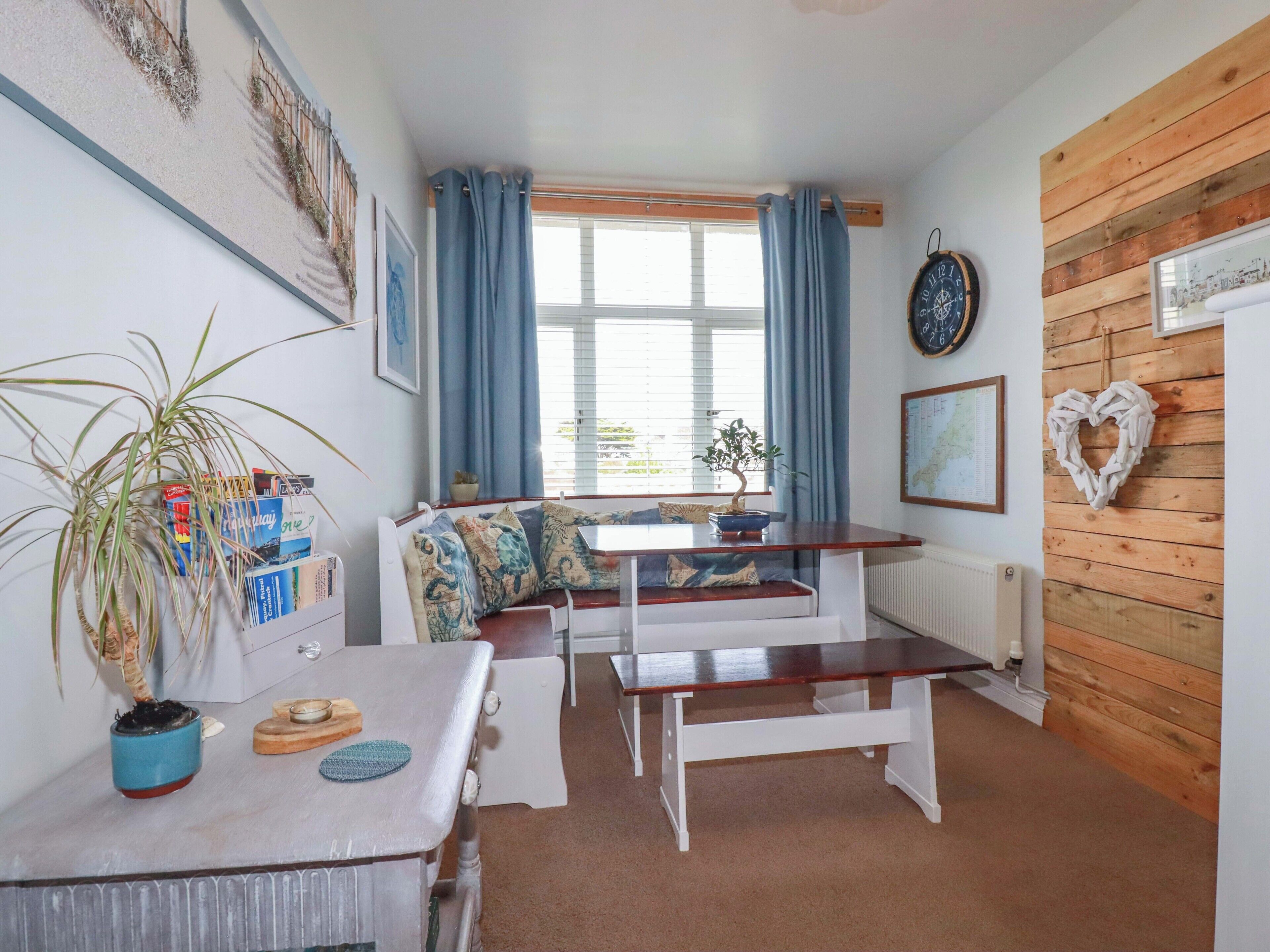 Quarto aconchegante com parede de madeira, um banco, uma mesa, uma planta em vaso e uma janela com cortinas.