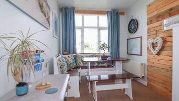 Quarto aconchegante com parede de madeira, um banco, uma mesa, uma planta em vaso e uma janela com cortinas.