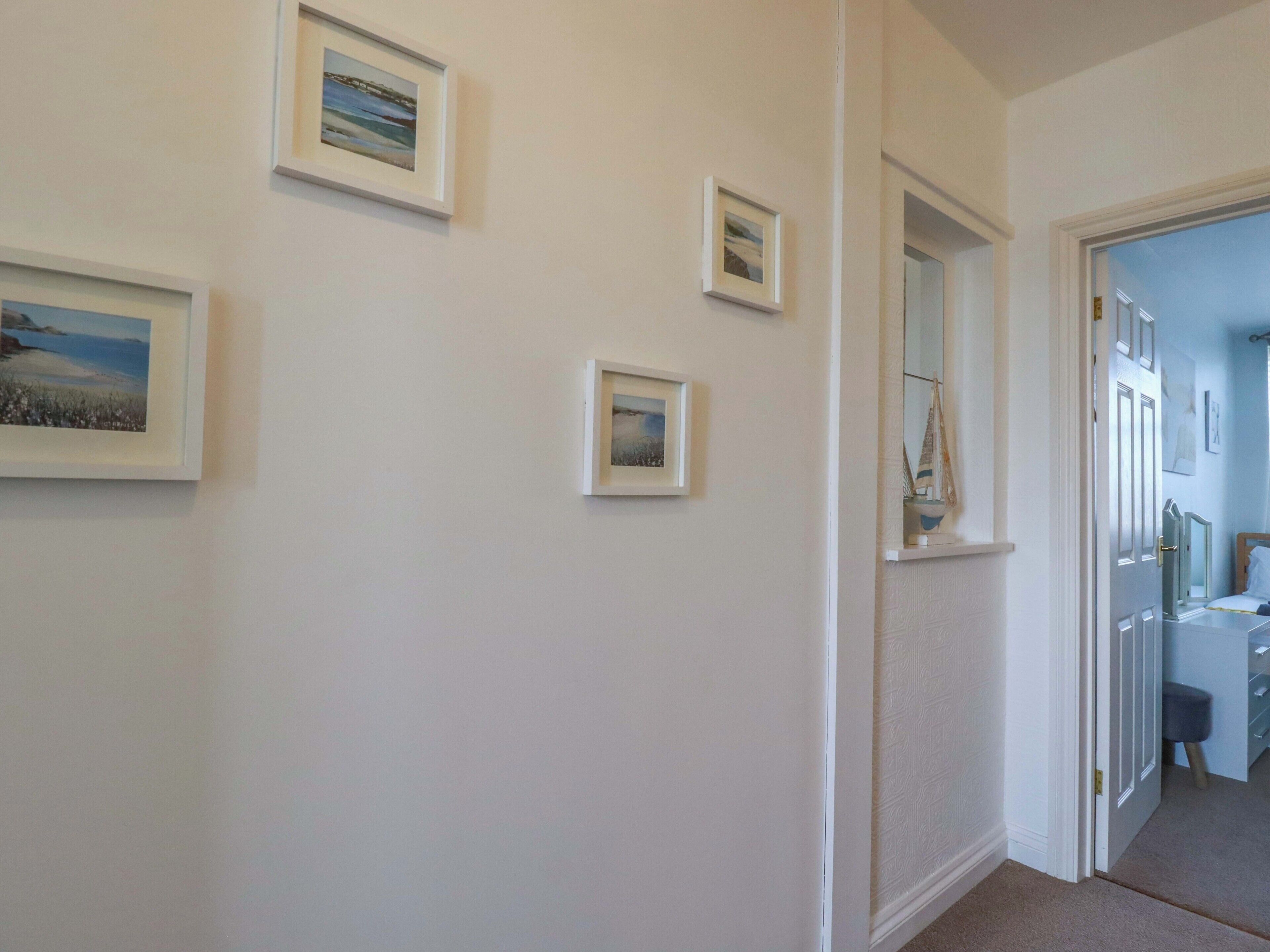 Um corredor com paredes brancas, quadros enquadrados e uma porta que dá para outro quarto.