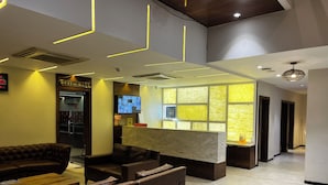 Um saguão de hotel com balcão de recepção, assentos de couro, um relógio digital e um letreiro de restaurante.