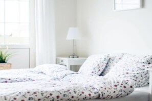 Quarto com cama, mesa de cabeceira, luminária e janela com cortinas.