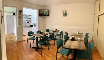 Uma área de refeições com televisão, uma cozinha ao fundo e piso de madeira.