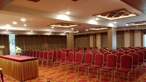 Sala de conferência com fileiras de cadeiras vermelhas, um púlpito e piso coberto de carpete.