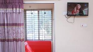 Quarto com janela, televisão na parede e sofá vermelho.