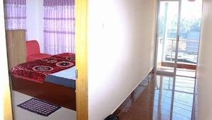 Quarto com cama, guarda-roupa, uma cadeira vermelha e porta de vidro deslizante para área externa.