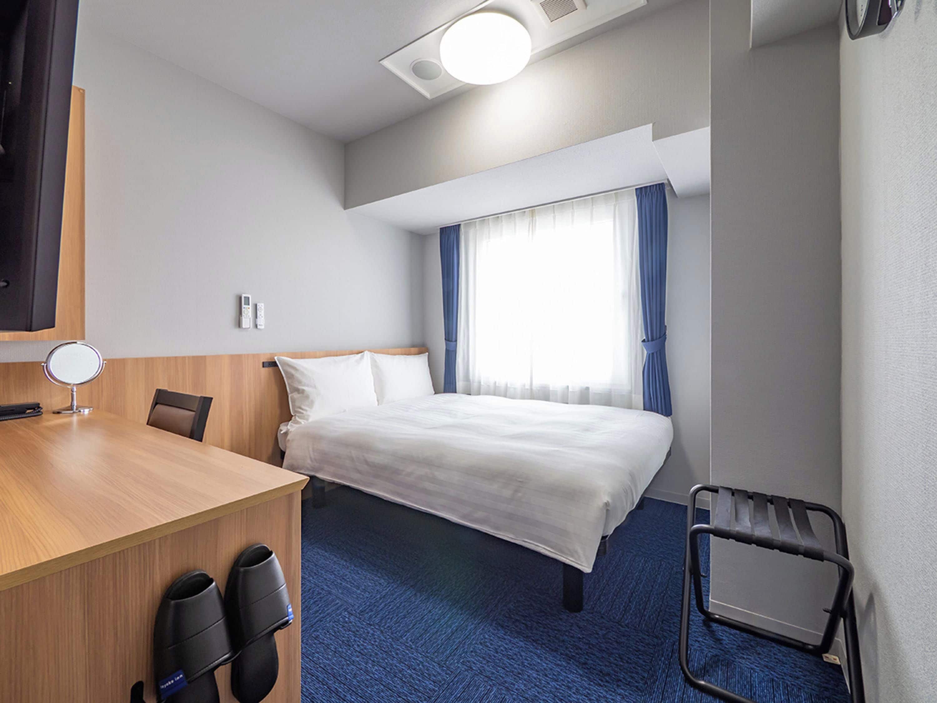 Quarto de hotel com cama, escrivaninha, cadeira, espelho e janela com cortinas.