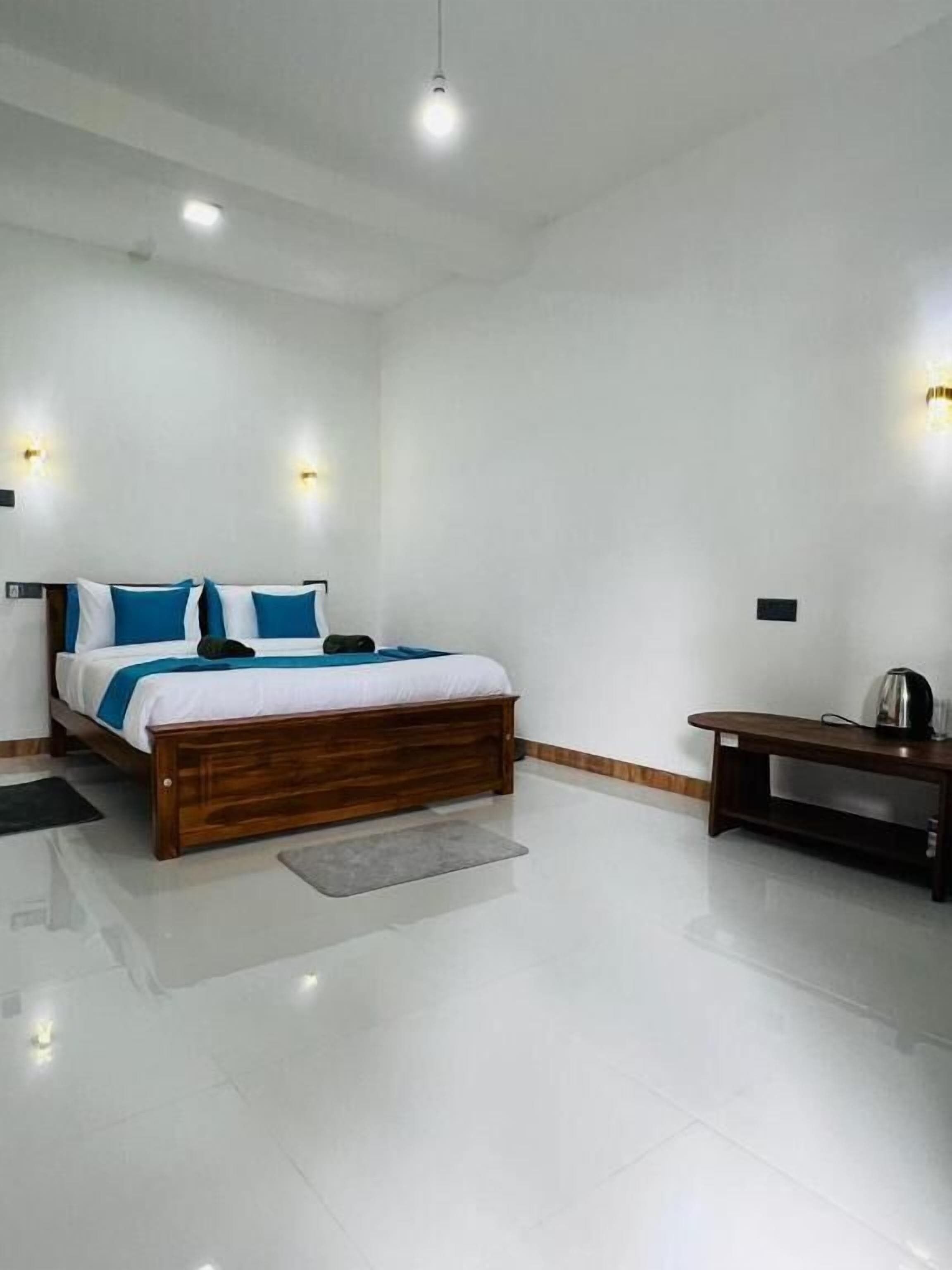 Quarto de hotel moderno com cama de madeira, paredes brancas e uma pequena mesa de cabeceira de madeira.