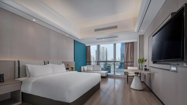 Quarto de hotel moderno com uma cama grande, uma TV, uma mesa de escritório e vista para a cidade.