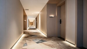 Um corredor de hotel com piso em carpete, portas em ambos os lados e um luminário na parede.