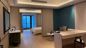 Quarto de hotel moderno com cama, escrivaninha, mesinha, televisão e janela com cortinas.
