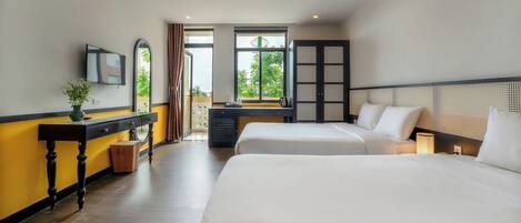 Quarto de hotel com duas camas, uma escrivaninha, televisão e vista para o verde lá fora.