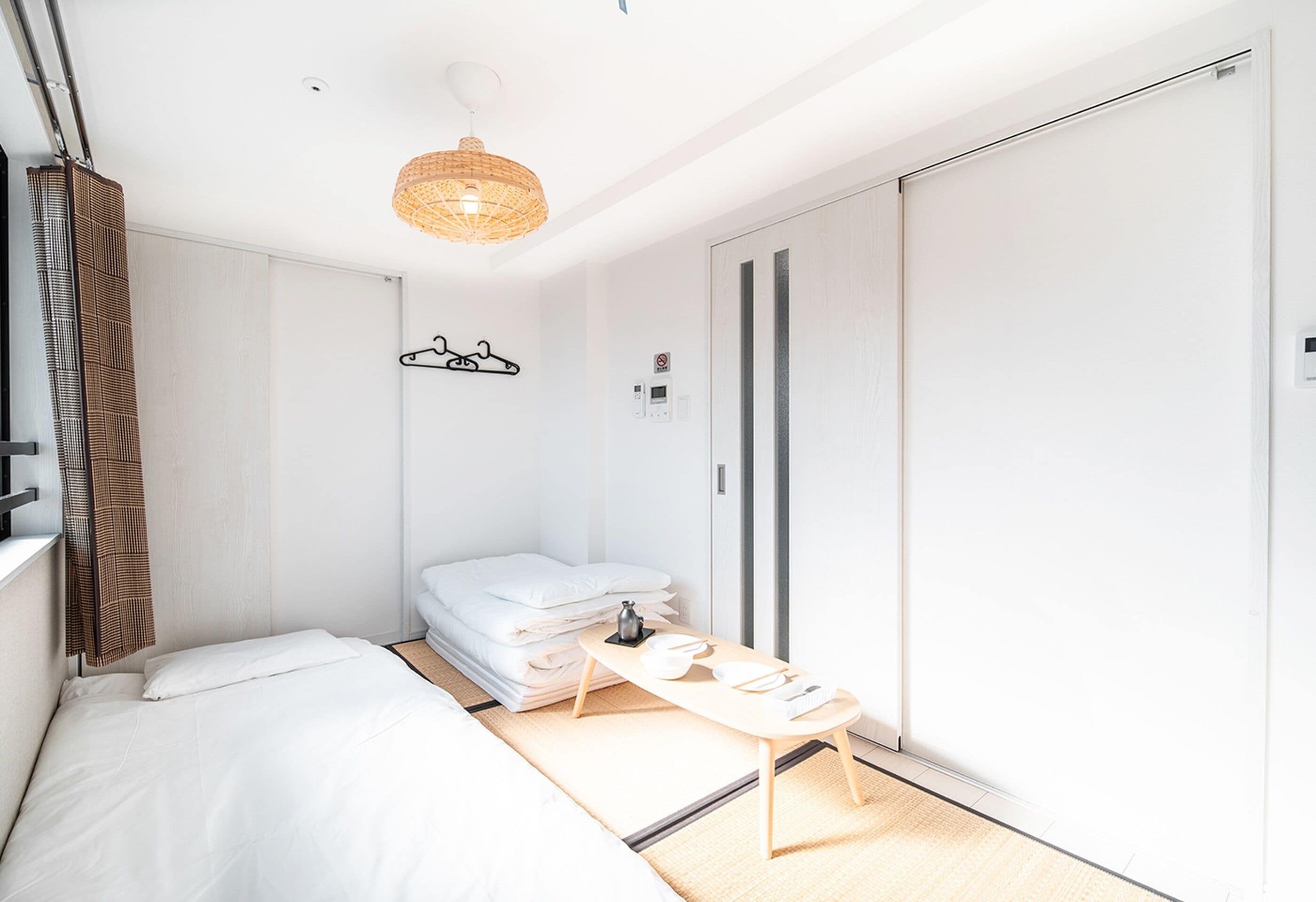 Quarto de hotel minimalista com uma cama, uma mesinha, um candeeiro suspenso e um guarda-roupa.