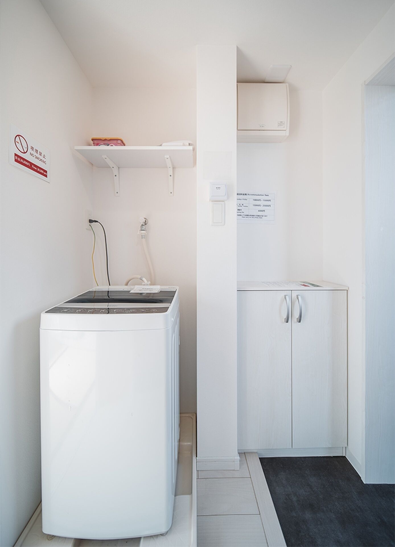 Quarto compacto com máquina de lavar, um pequeno armário, uma prateleira com objetos e ar condicionado fixado na parede.