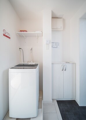 Quarto compacto com máquina de lavar, um pequeno armário, uma prateleira com objetos e ar condicionado fixado na parede.