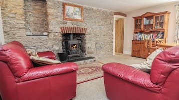 Uma sala de estar aconchegante com parede de pedra, lareira, poltronas de couro vermelho e estante de madeira.