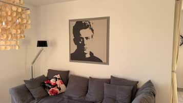 Uma sala de estar com um sofá cinzento, um abajur preto e um retrato emoldurado na parede.